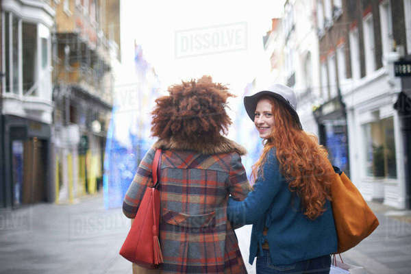 Two young women, walking arm in arm in street - Stock Photo - Dissolve