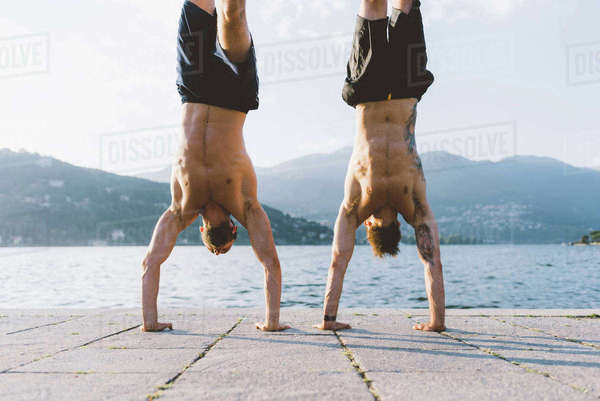 Two young men doing handstands on waterfront, Lake Como, Lombardy ...