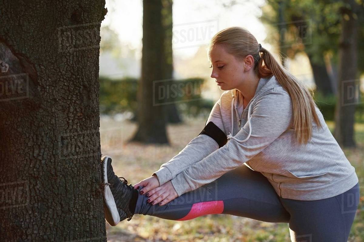 Curvaceous young woman training in park, touching toes against tree ...