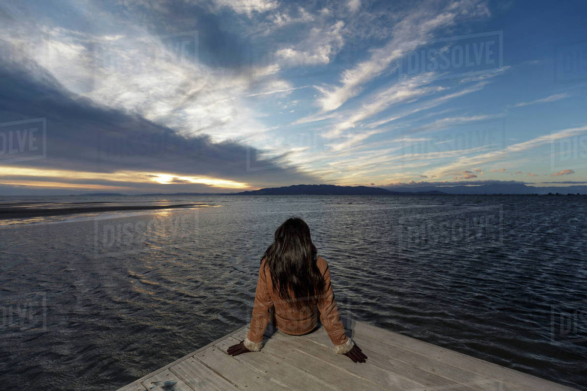 Young woman looking out from pier at sunset, Tarragona, Catalonia ...