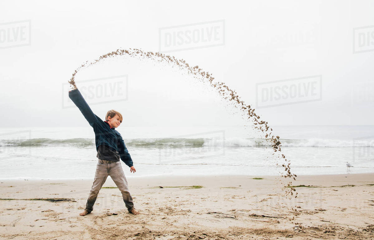 Portrait of young boy on beach, throwing sand in arch shape - Stock ...