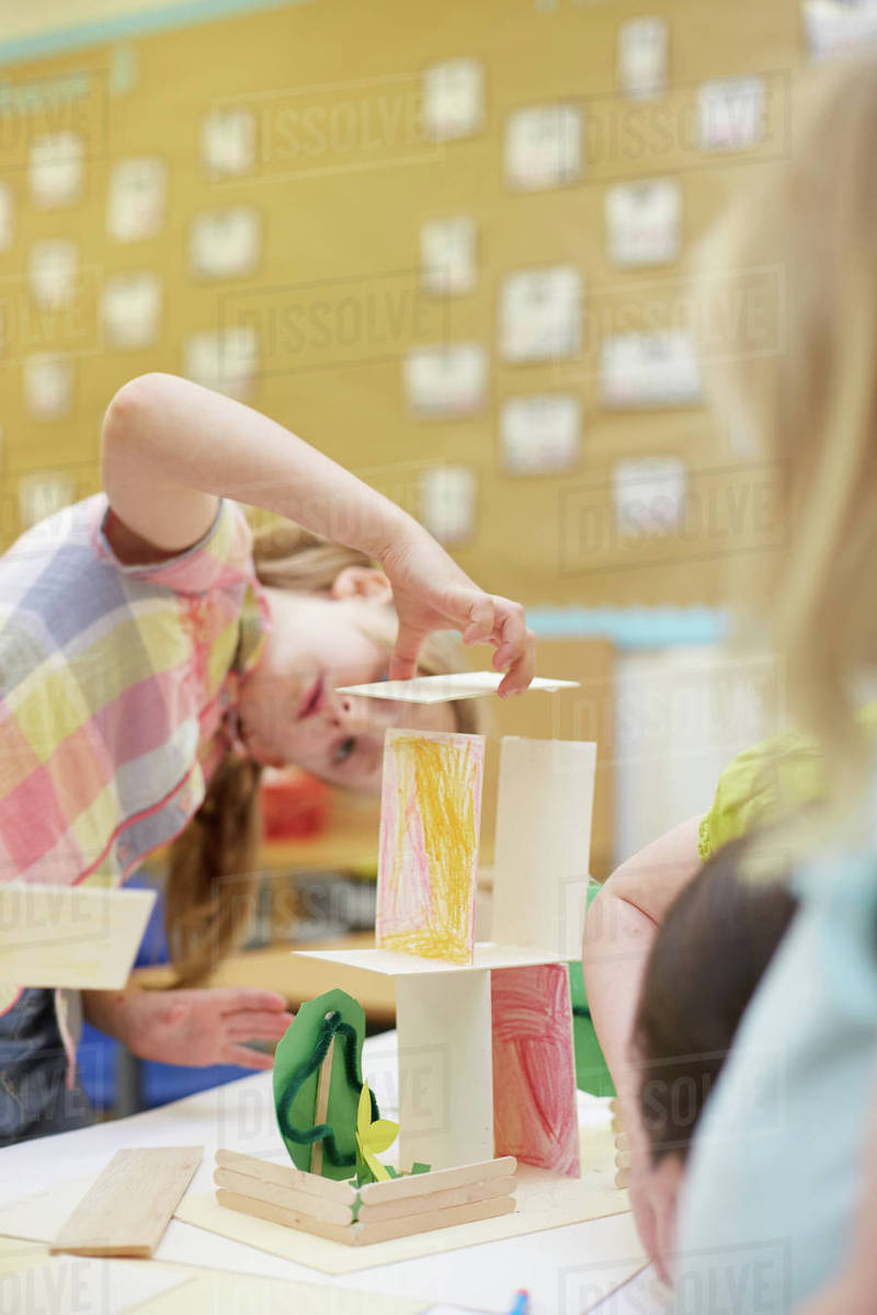 Primary schoolgirl making a cardboard structure on classroom desks ...