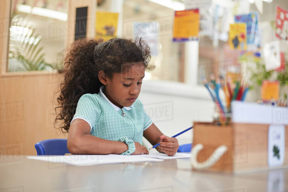 Schoolgirl writing at classroom desk in primary school - Royalty-free ...