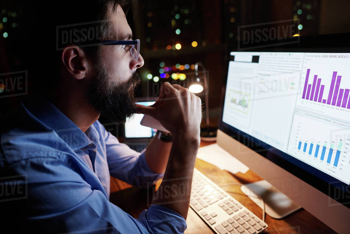Young businessman looking at computer on office desk at night - Royalty ...