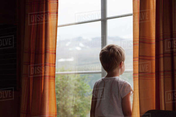 Boy looking through curtained window - Stock Photo - Dissolve