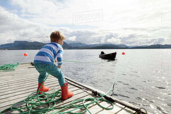 Boy on pier pulling fjord boat by rope, Aure, More og Romsdal, Norway ...