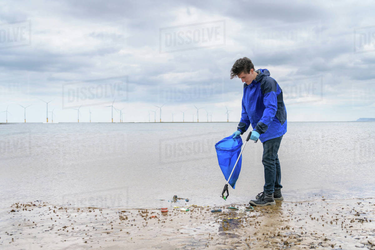Man using litter picker to remove plastic pollution collected on beach ...