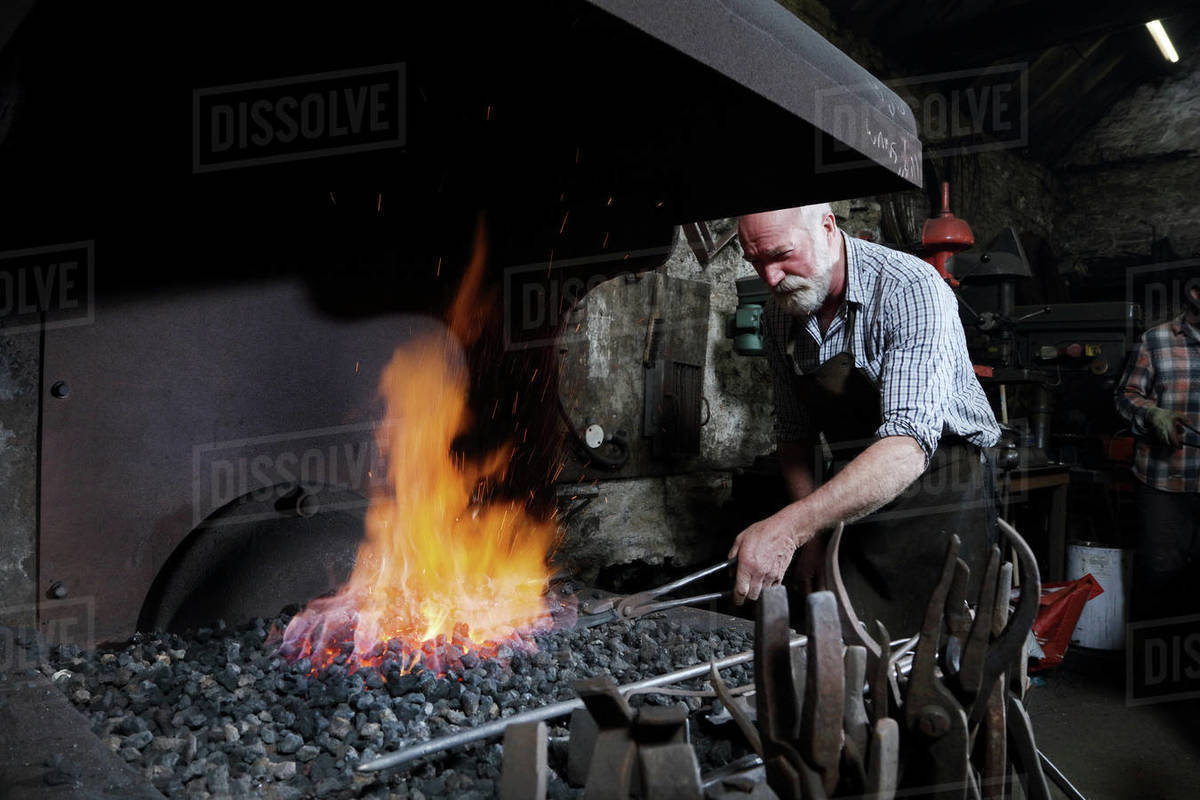 Blacksmith heating metal in forge fire in blacksmiths shop - Royalty ...