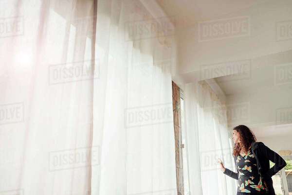 Woman peering out through net curtained window - Stock Photo - Dissolve