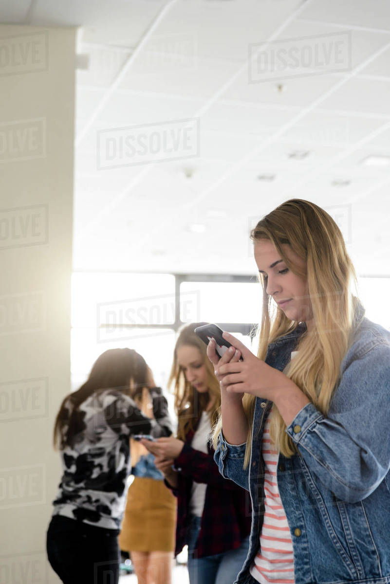 Female students looking at smartphones in university corridor - Stock ...