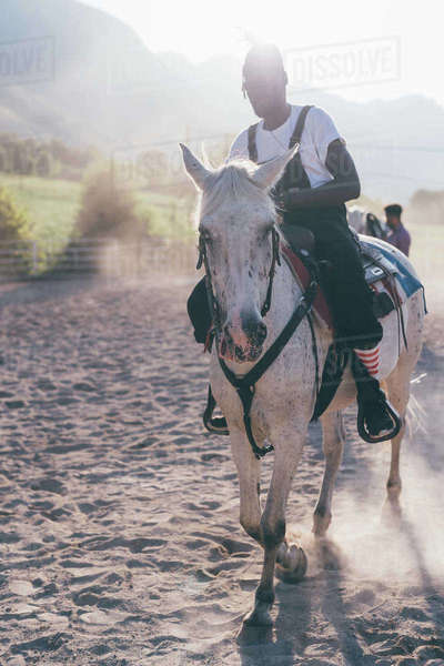 Young hipster man riding horse in sunlit equestrian arena, Primaluna ...