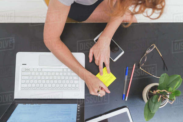 Businesswoman writing sticky notes on office desk, overhead view ...