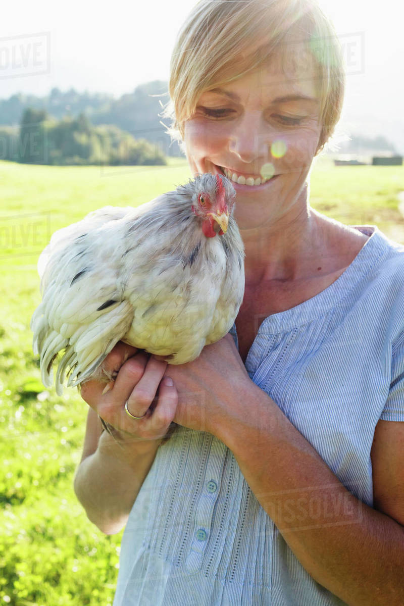 Woman carrying rooster in countryside - Royalty-free Stock Photo | Dissolve