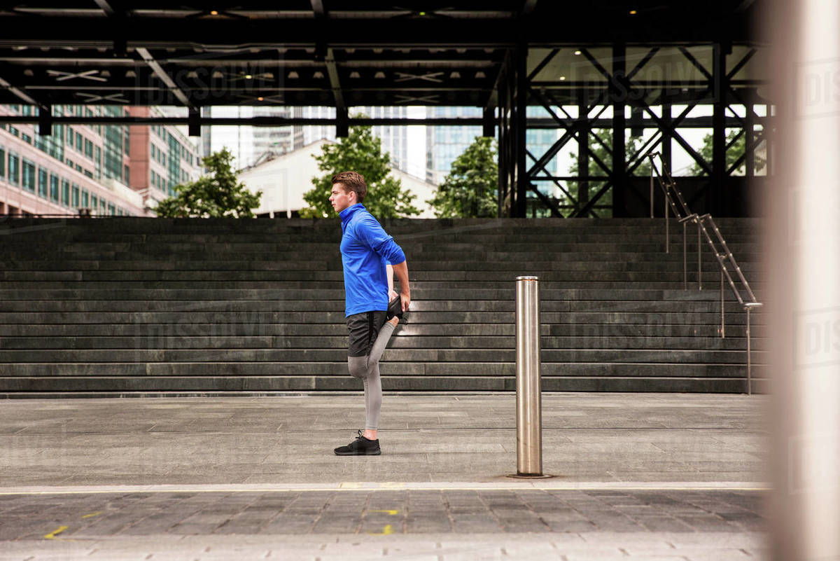 Young runner stretching on pavement, London, UK - Stock Photo - Dissolve
