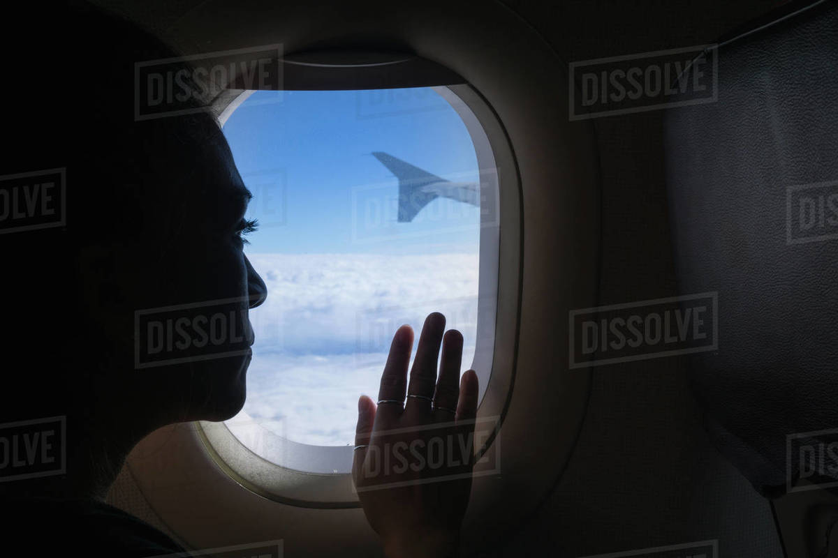 Woman travelling in airplane, looking out window - Stock Photo - Dissolve