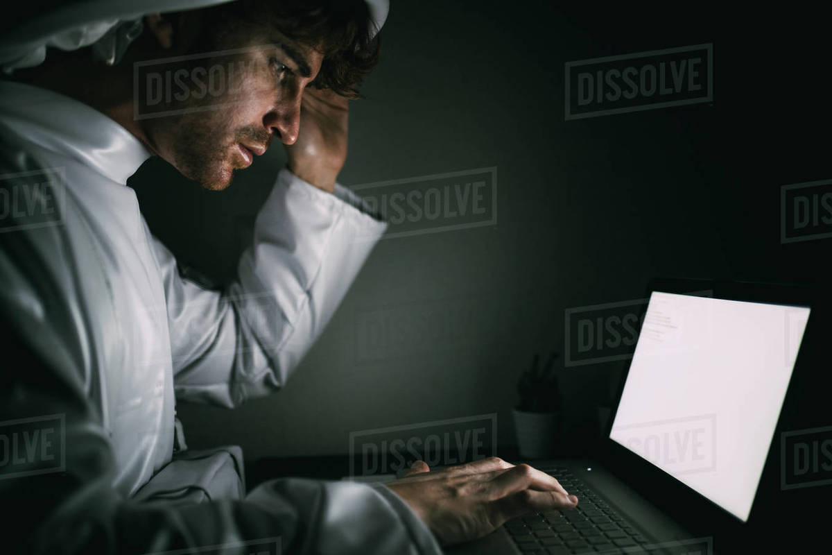 Astronaut using laptop in dark room - Stock Photo - Dissolve