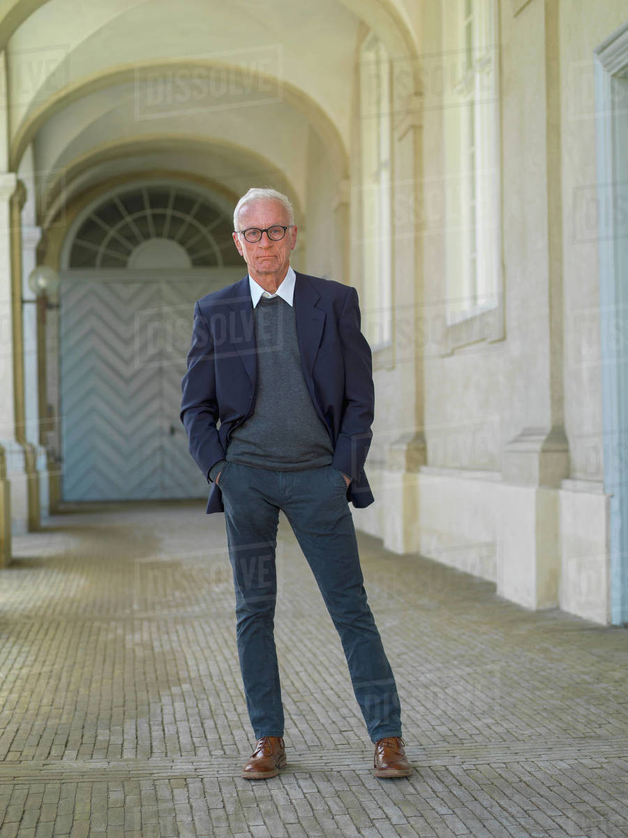 Senior man in suit jacket standing in traditional portico, portrait ...