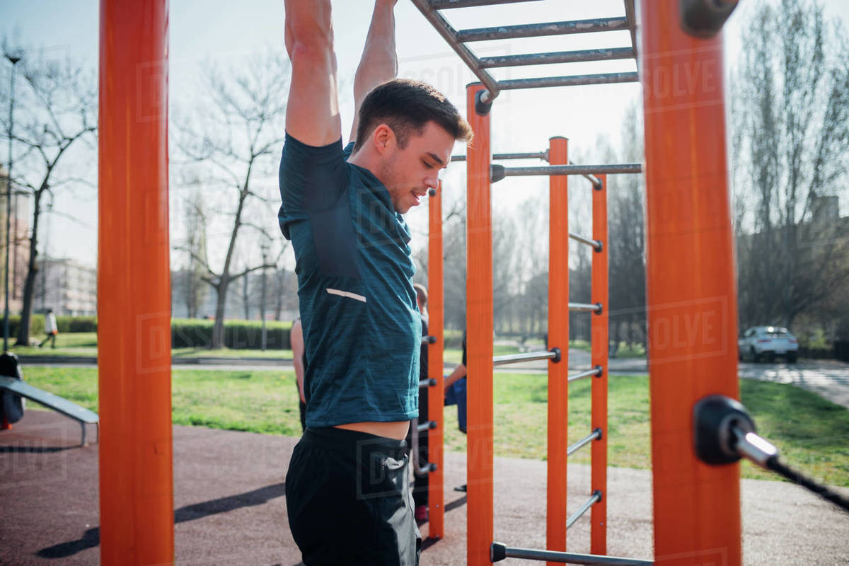 Calisthenics at outdoor gym, young man hanging from exercise equipment ...