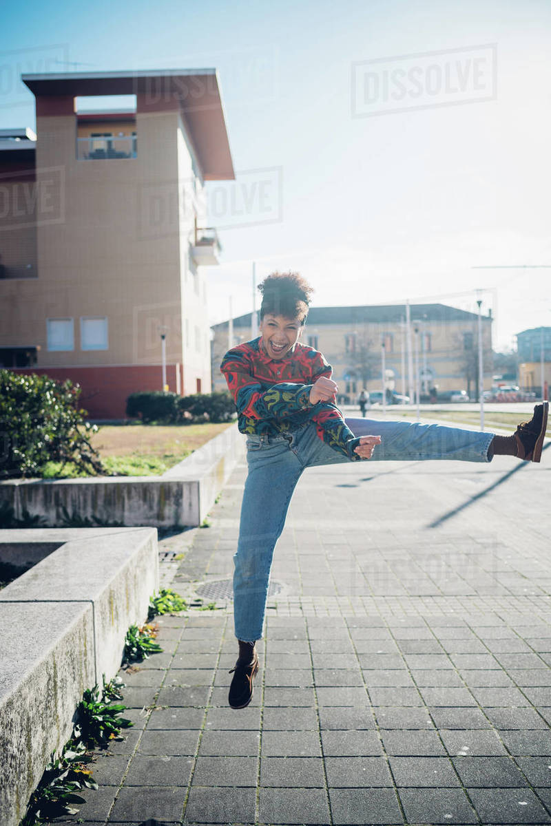 Young woman jumping and kicking leg on urban sidewalk, full length ...