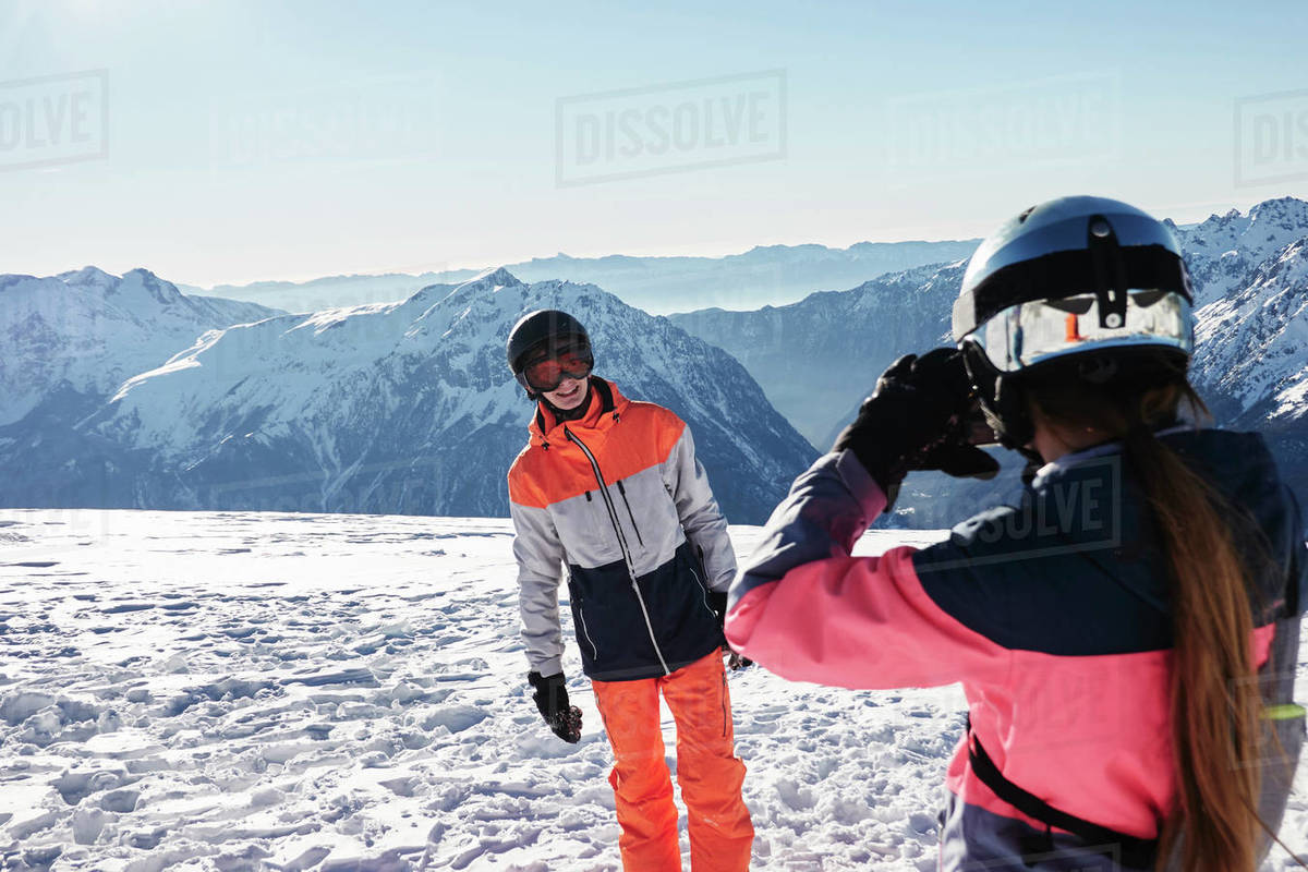 Teenage girl skier taking photo of teenage brother on snow covered ...