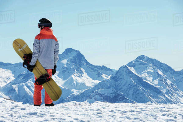 Teenage boy snowboarder looking out over landscape from snow covered ...