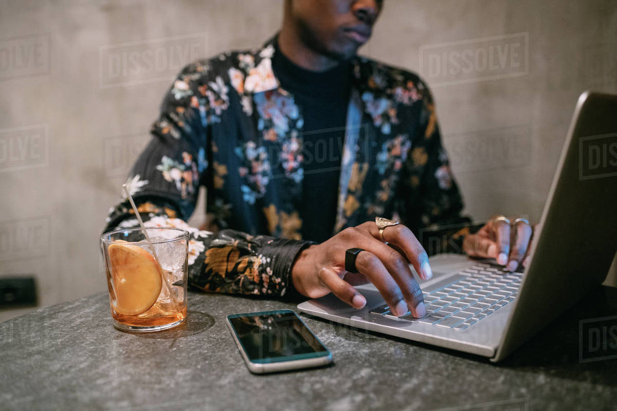 Stylish man enjoying drink while using laptop - Royalty-free Stock ...