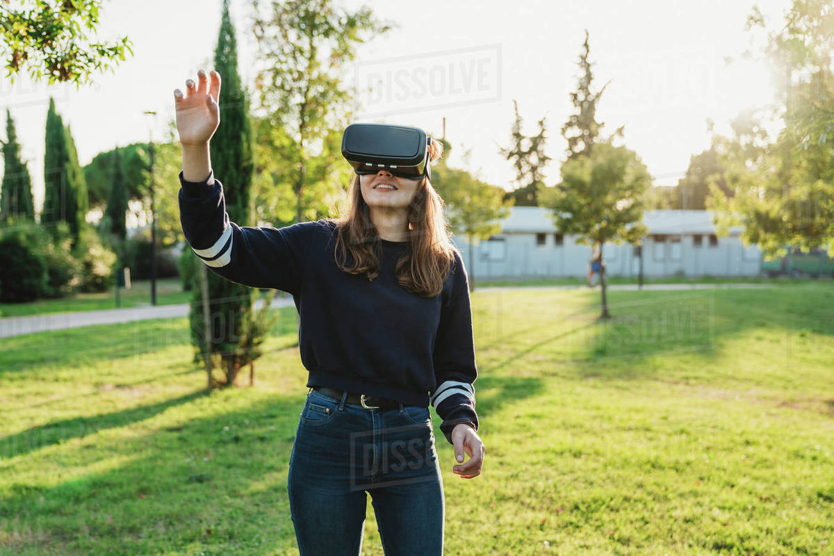 Young woman looking through VR headset in park - Stock Photo - Dissolve