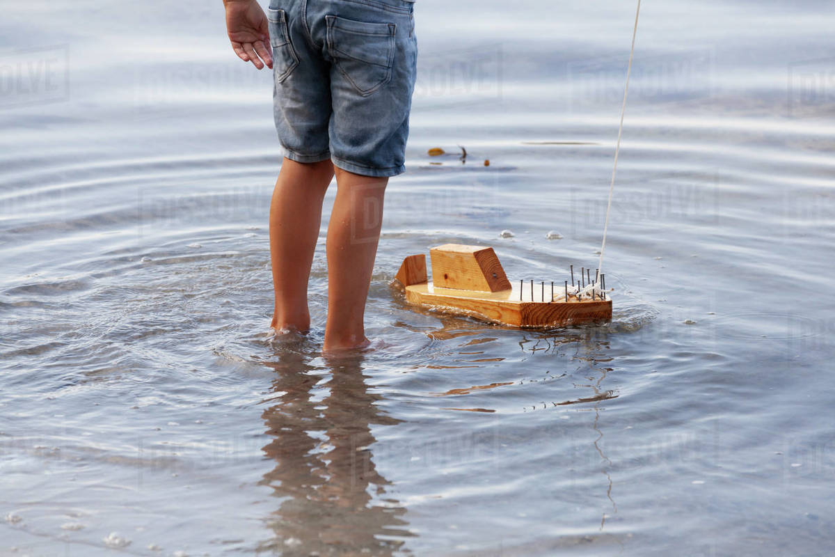 Boy playing with wooden toy boat in water - Royalty-free Stock Photo ...