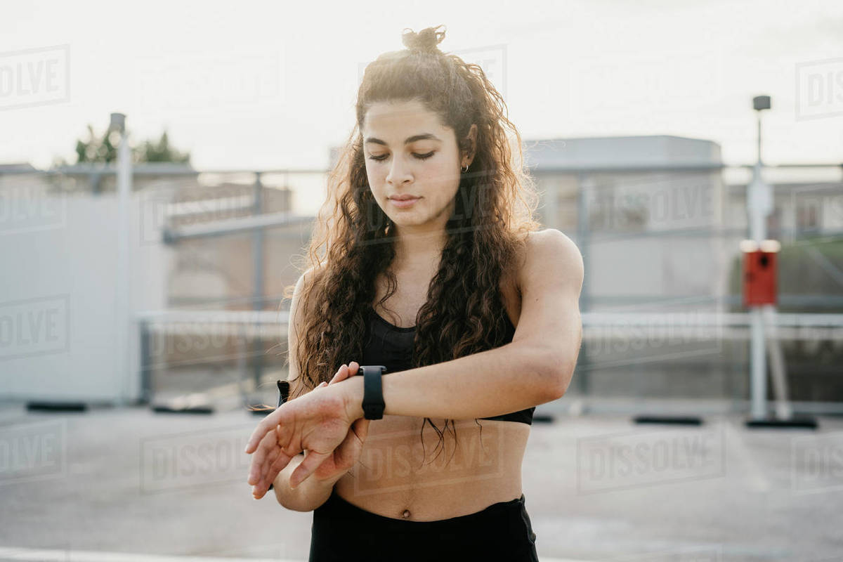 Young woman checking smartwatch on rooftop deck - Stock Photo - Dissolve