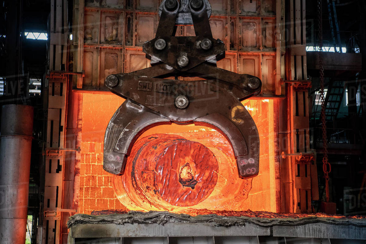 Heat treated red hot steel ingot being lifted by crane in furnace in ...