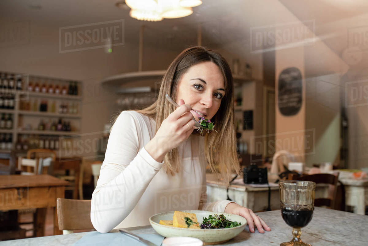 A woman seated at a cafe table eating a dish of vegan food, vegetables ...