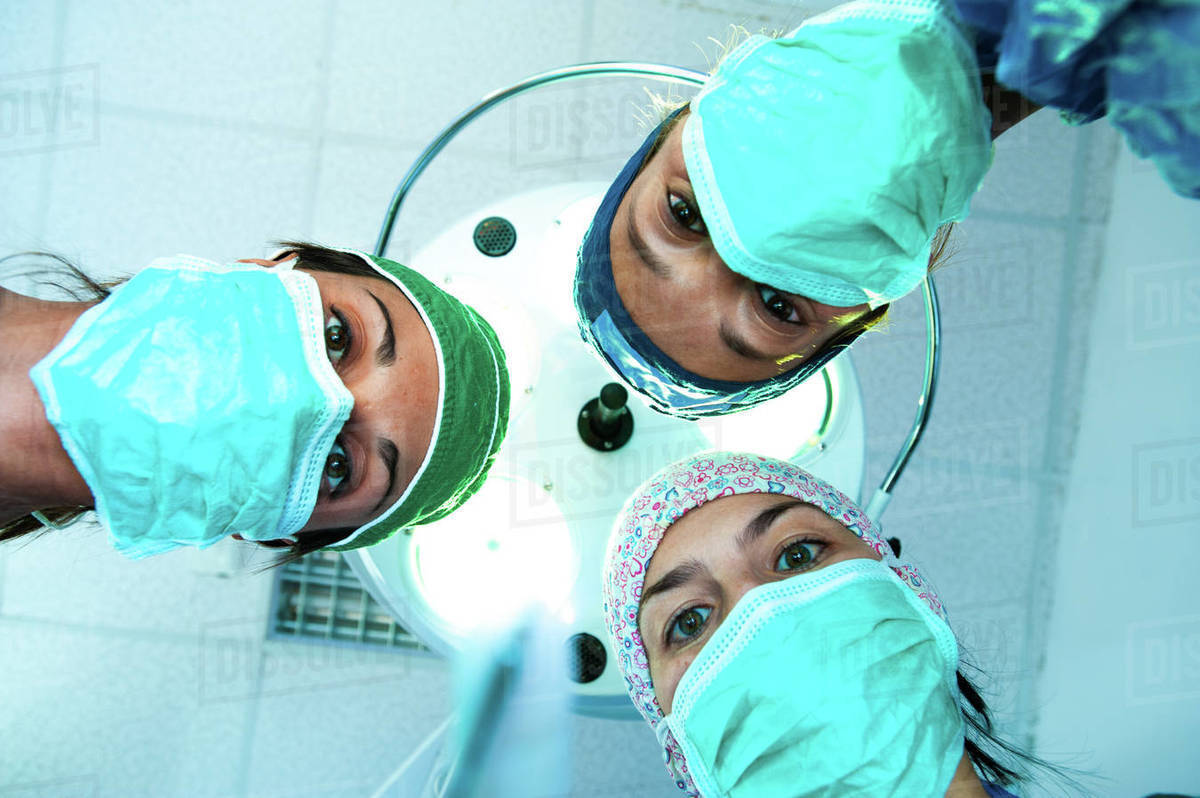 Low angle view of three female surgeons wearing surgical masks looking ...