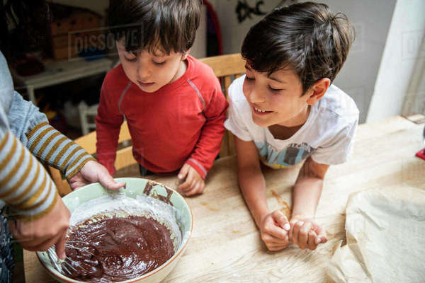 Two boys with black hair sitting at a kitchen table, baking chocolate ...