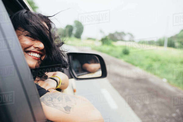 Smiling woman with long brown hair and tattoos looking out of car ...