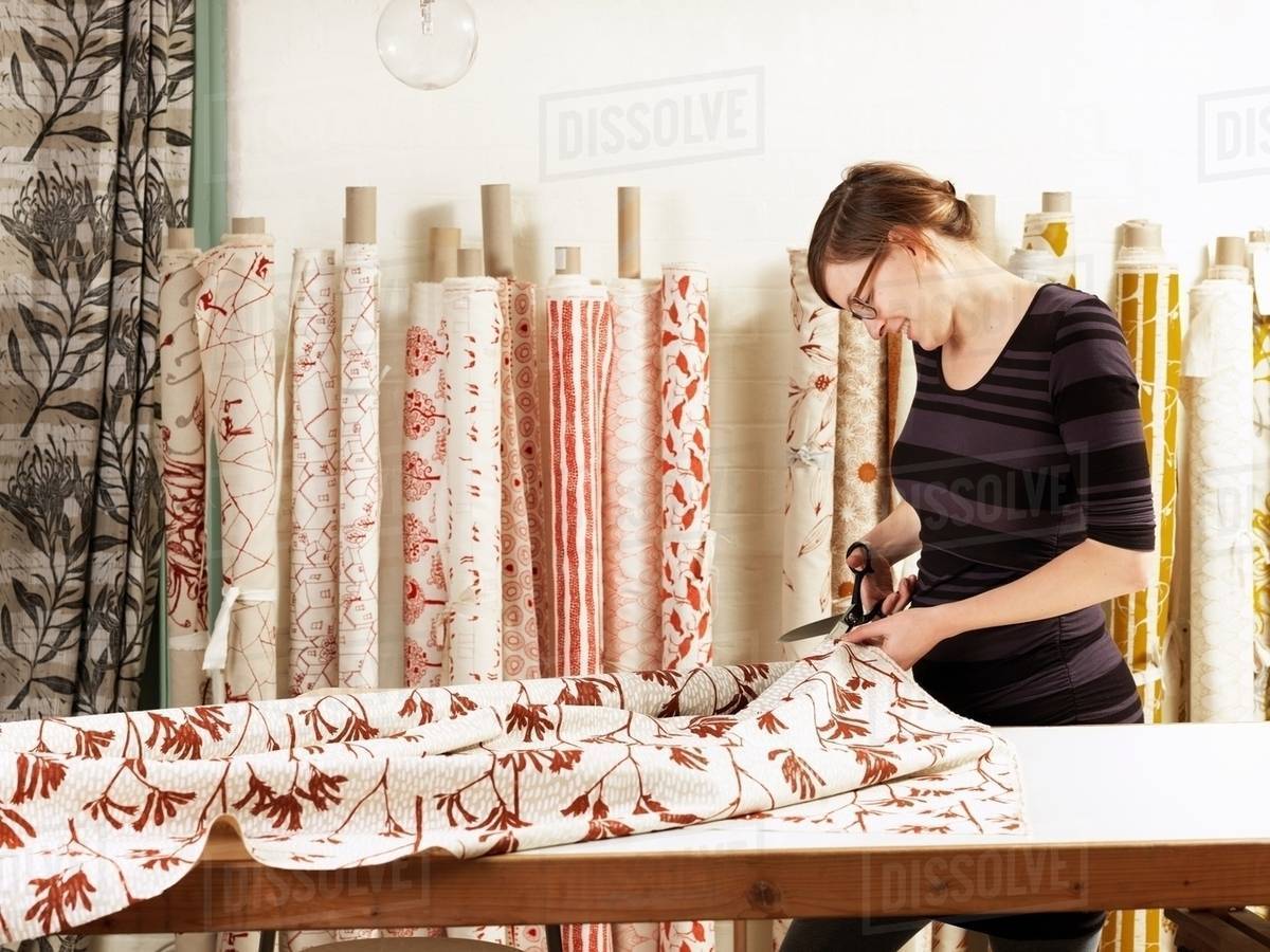 Woman cutting fabric on work table in hand-printed textile workshop ...