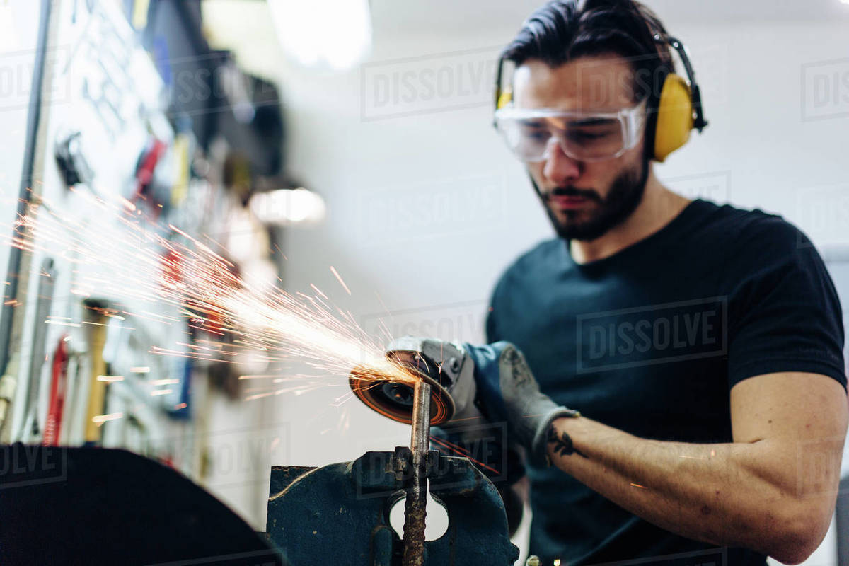 Young man using angle grinder on metal in workshop - Stock Photo - Dissolve