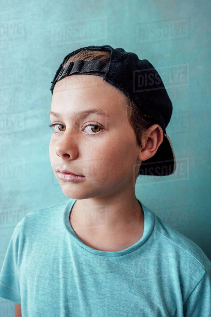 Portrait of boy wearing baseball cap, looking at camera, on blue ...
