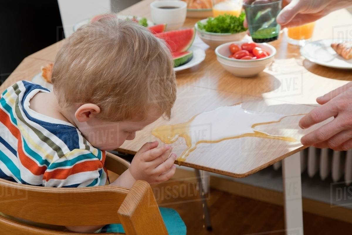 Male toddler accidentally spilling orange juice at breakfast table ...