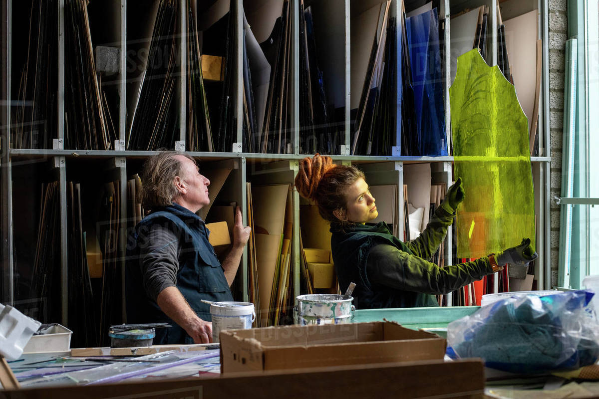 Male and female stained glass workers inspecting coloured glass ...