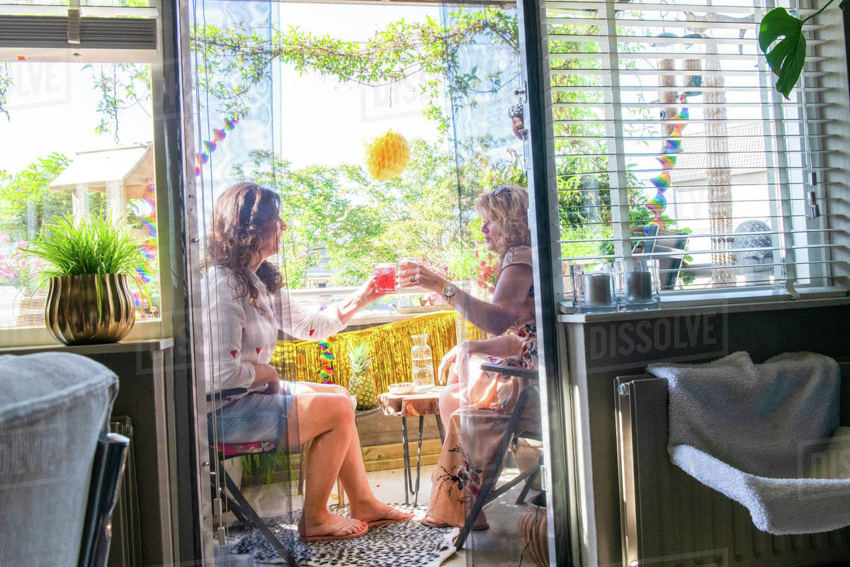 Two friends sitting on the balcony on a summers day drinking cocktails ...