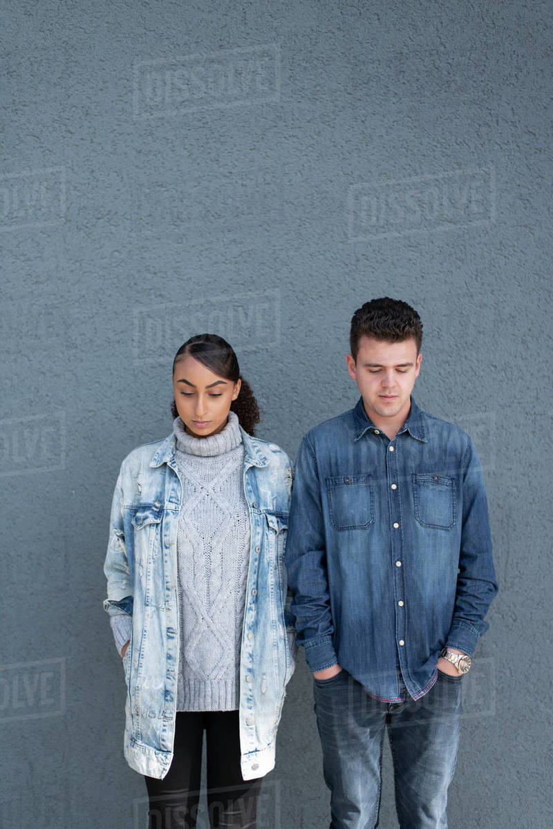 White male and mixed race female colleagues standing again a wall with ...