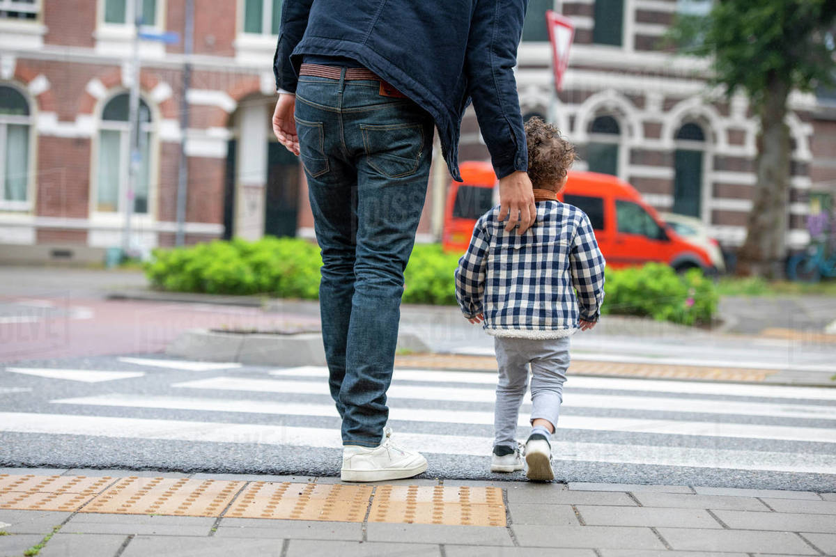 A parent and child holding hands while crossing the street on a cloudy ...