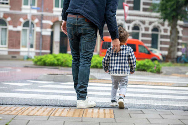 A parent and child holding hands while crossing the street on a cloudy ...