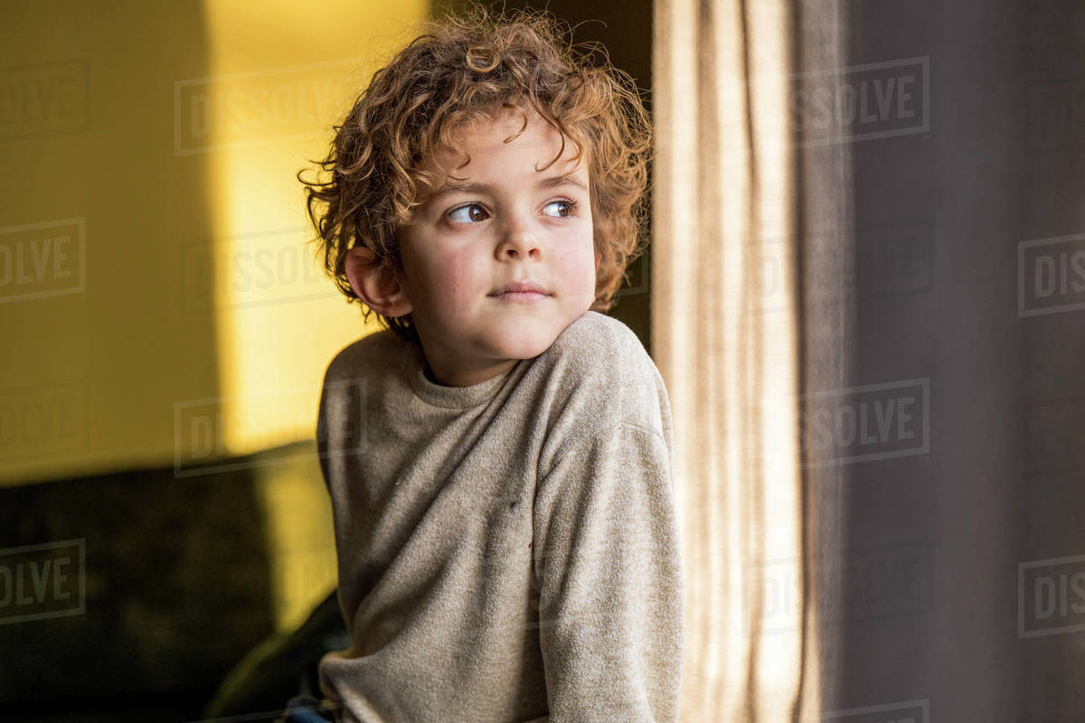 Curious child gazing out the window with a thoughtful expression ...