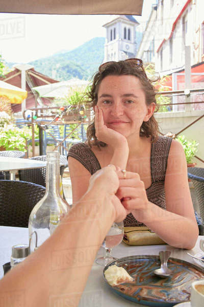 A smiling woman is sitting at an outdoor dining table; her chin is ...