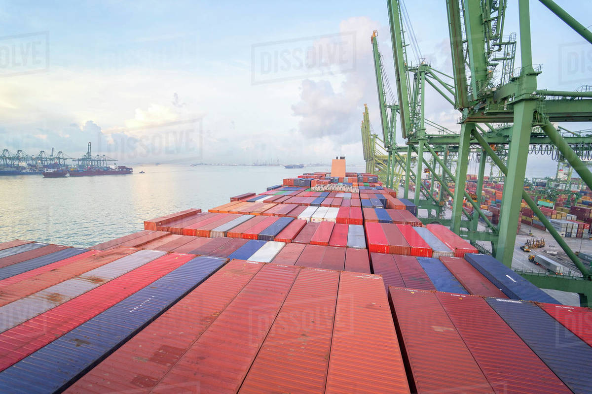 A container ship is docked at a busy port with a clear sky at dawn or ...