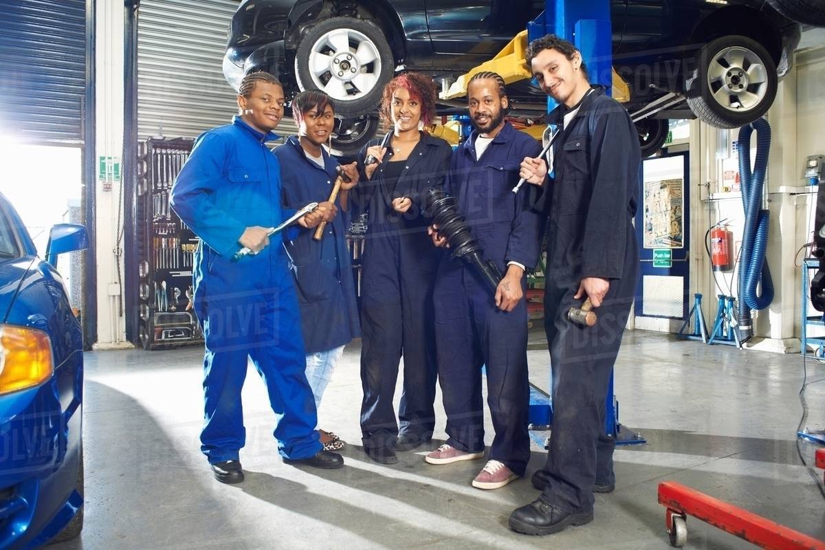 Portrait of five college students beneath car in garage workshop ...