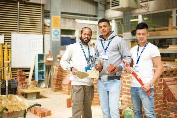 Portrait of three male college students in bricklaying workshop ...