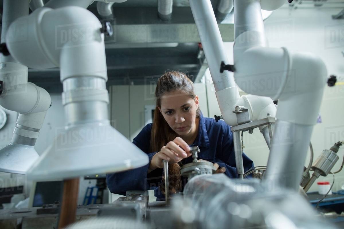 Female engineer turning pipe valves in factory - Stock Photo - Dissolve