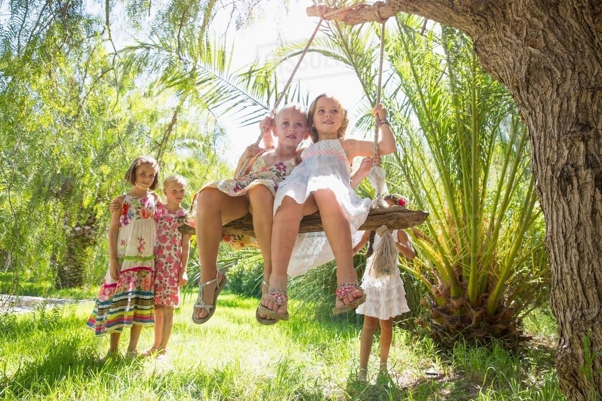 Five girls playing with tree swing in garden - Stock Photo - Dissolve